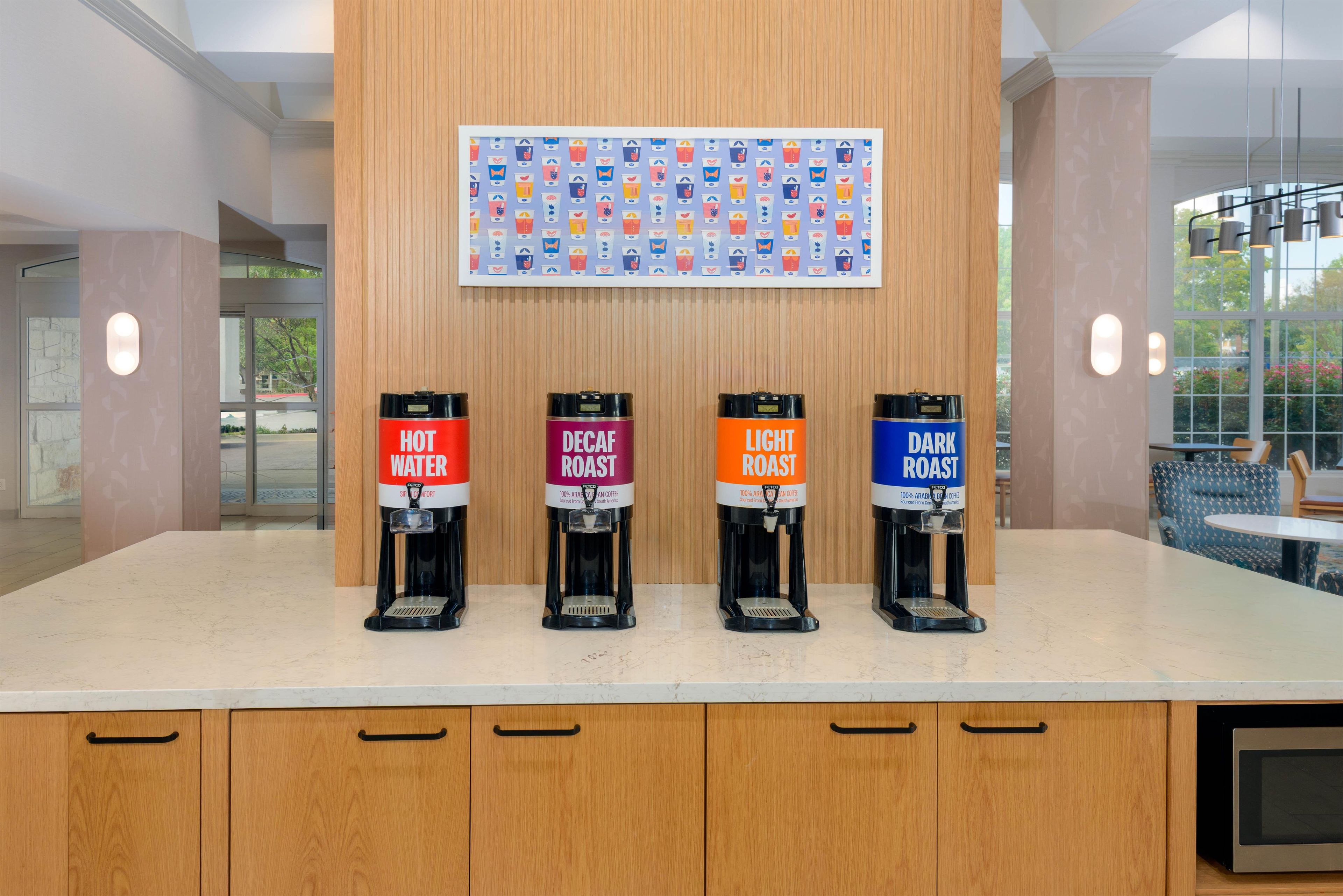 Estação de café com quatro dispensadores rotulados 'ÁGUA QUENTE', 'ROAST DECAF', 'ROAST CLARO' e 'ROAST ESCURO'.