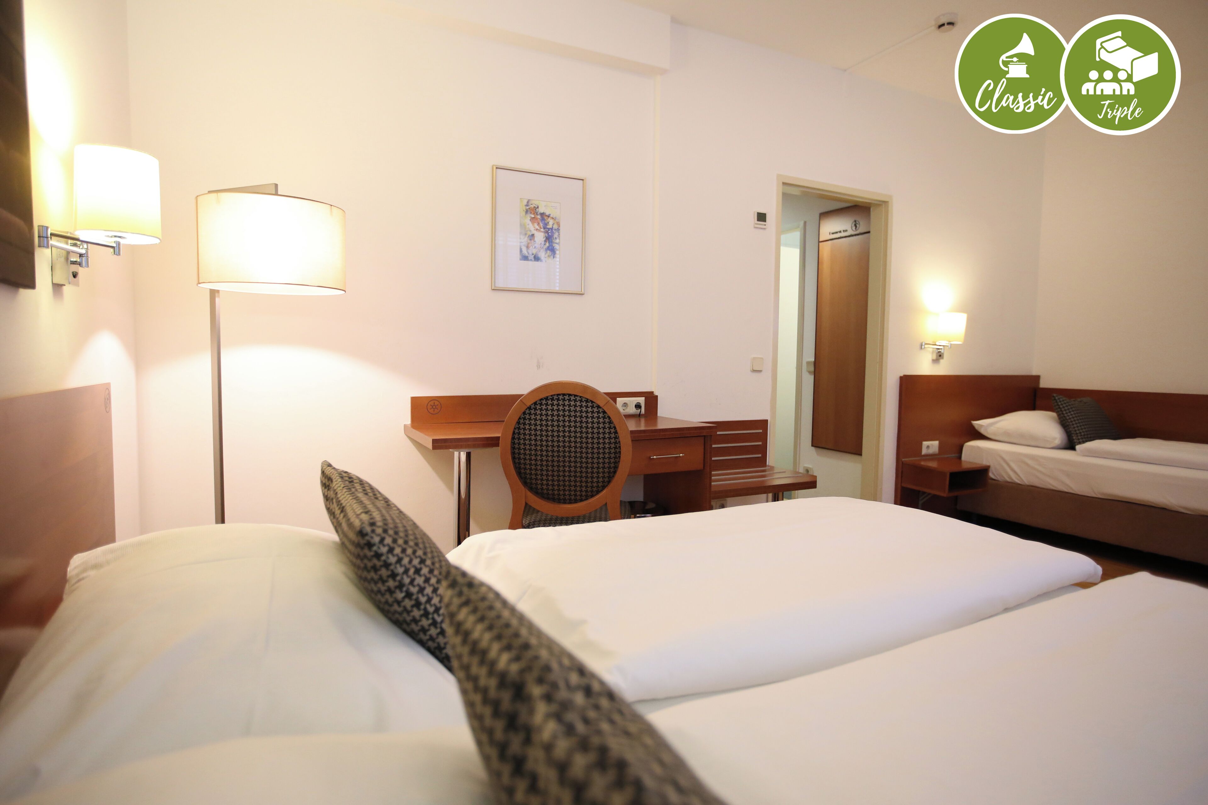 Quarto de hotel com cama, escrivaninha, cadeira e luminária.
