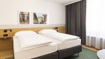 Quarto de hotel com duas camas, cabeceira de madeira, tapete verde e duas imagens emolduradas na parede.