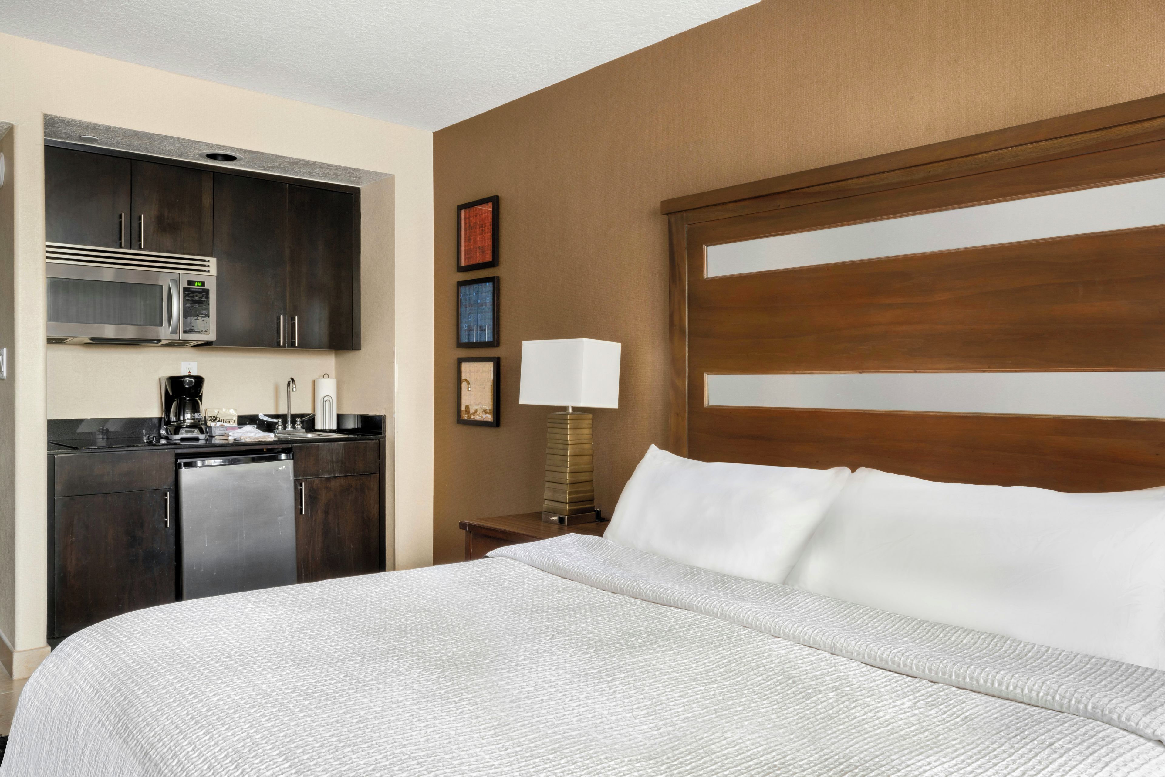 Quarto de hotel com uma cama, uma mesa com abajur, micro-ondas e cafeteira.