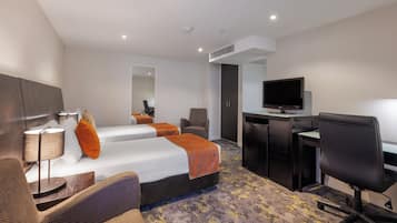 Quarto de hotel com cama, duas mesas de cabeceira, escrivaninha com cadeira, televisão e banheiro.