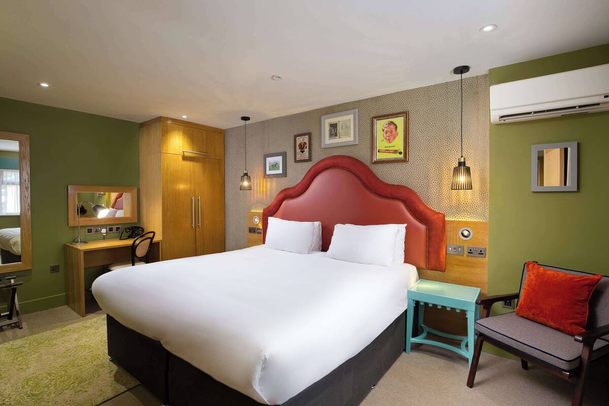 Quarto de hotel com uma cama grande, uma escrivaninha, uma cadeira e uma mesa pequena.