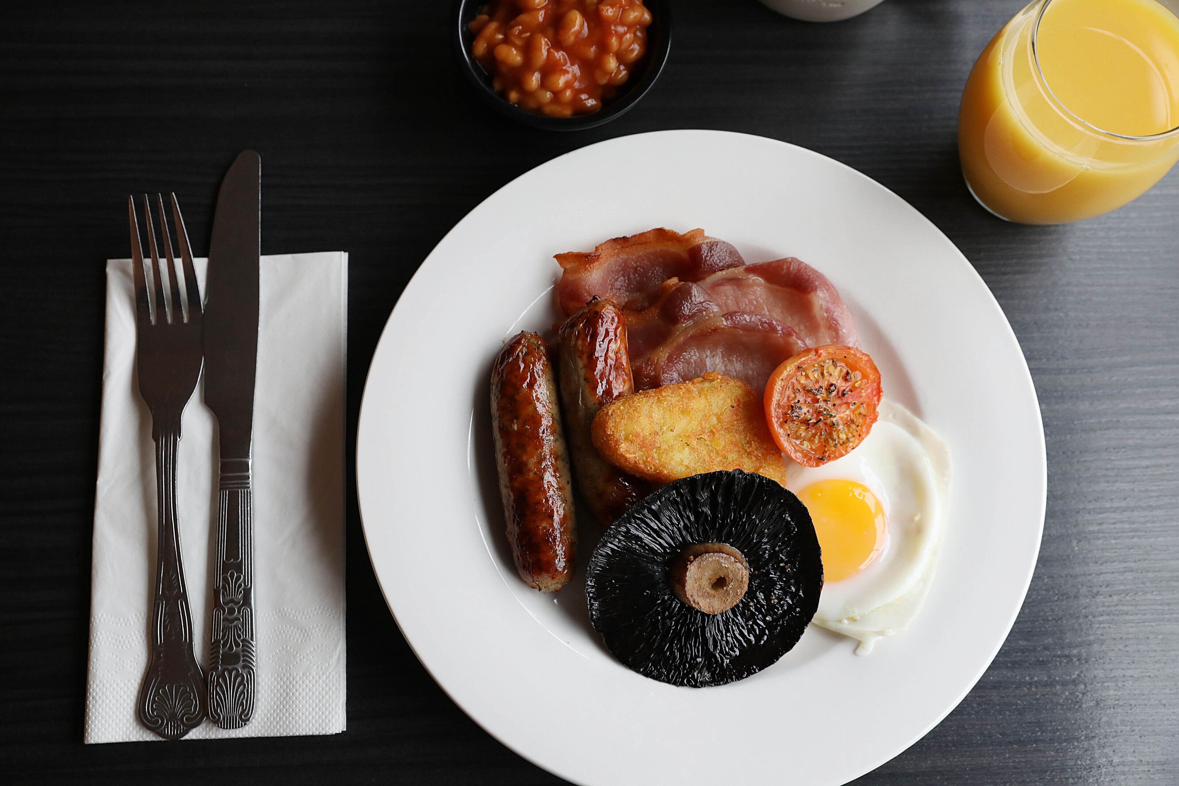 Prato de comida de café da manhã com linguiça, bacon, ovos e feijão cozido.