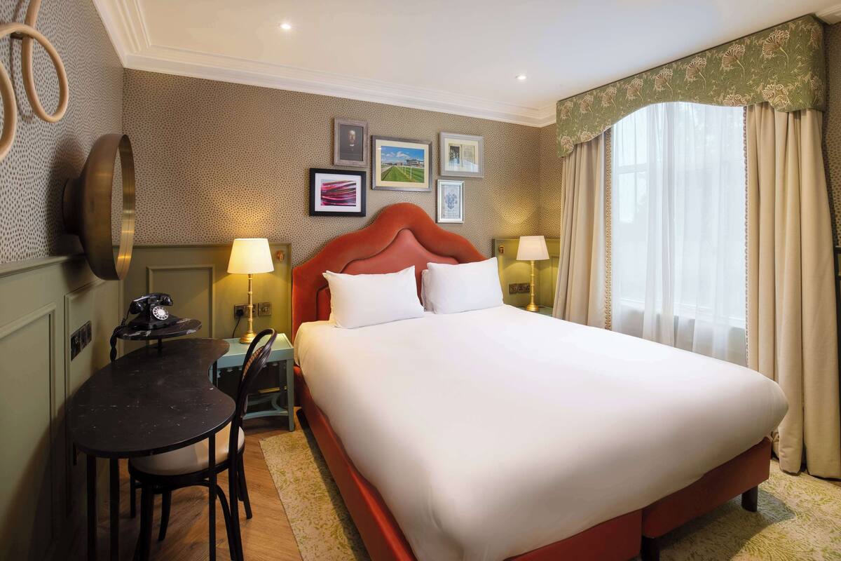 Quarto de hotel com uma cama grande, uma escrivaninha com cadeira, telefone e quadros nas paredes.