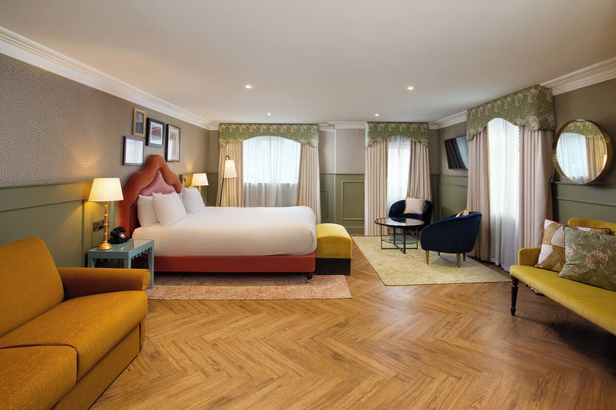 Quarto de hotel com cama, duas poltronas, um sofá, uma mesinha e um espelho.