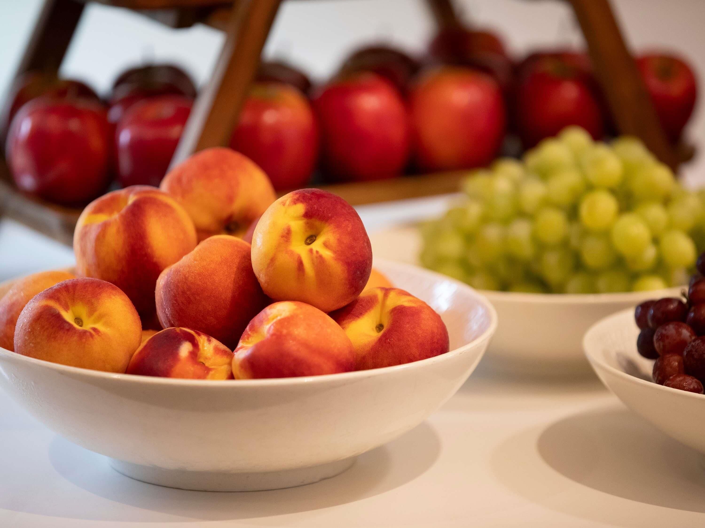 Uma tigela de pêssegos, uma tigela de uvas e uma tigela de cerejas sobre uma mesa.