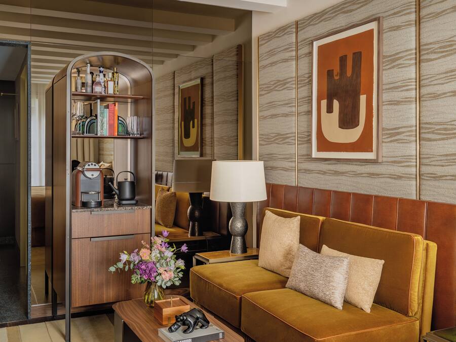 Quarto de hotel moderno com sofá, mesa de centro, estante de livros e uma grande pintura abstrata na parede.