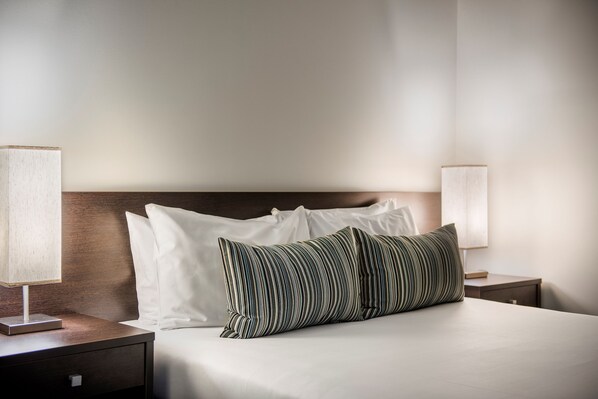 Cama bem arrumada com travesseiros brancos e listrados, cabeceira de madeira e luminárias de cabeceira em um criado-mudo de madeira escura.