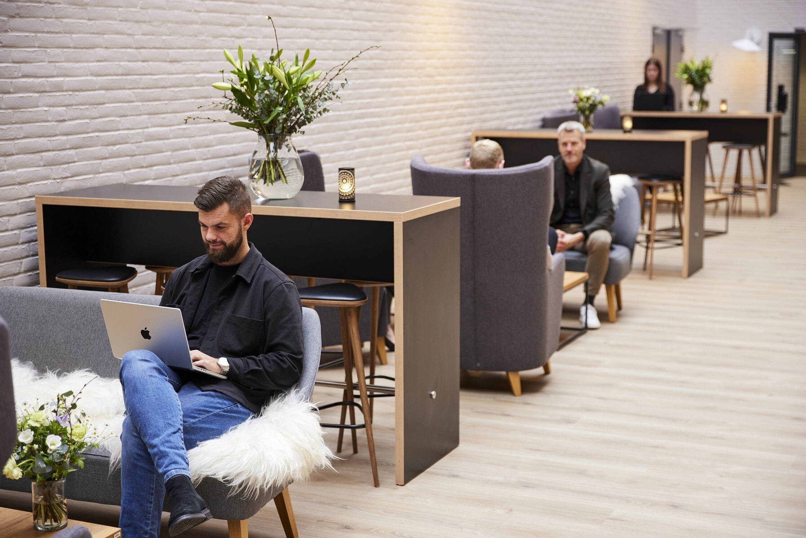 Uma área de lounge moderna com assentos e mesas, destacando uma parede de tijolos e piso de madeira.