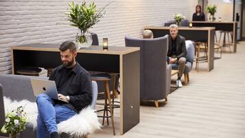 Uma área de lounge moderna com assentos e mesas, destacando uma parede de tijolos e piso de madeira.