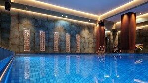 Piscina interior moderna com chão de azulejos azuis, painéis decorativos na parede e um pilar de madeira.