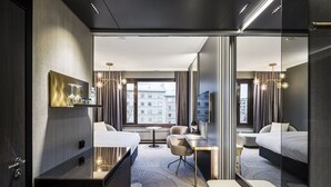 Quarto de hotel moderno com uma cama grande, uma escrivaninha, uma cadeira, uma mesinha e uma televisão.