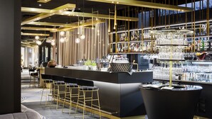 Uma área de bar moderna com balcão preto, detalhes dourados e um grande cachepot.