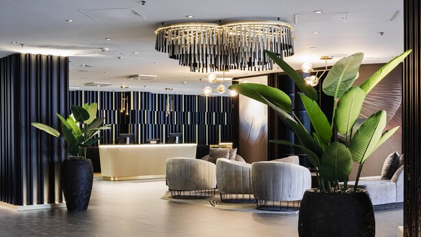 Um lobby moderno com balcão de atendimento, assentos confortáveis e grandes plantas em vasos.