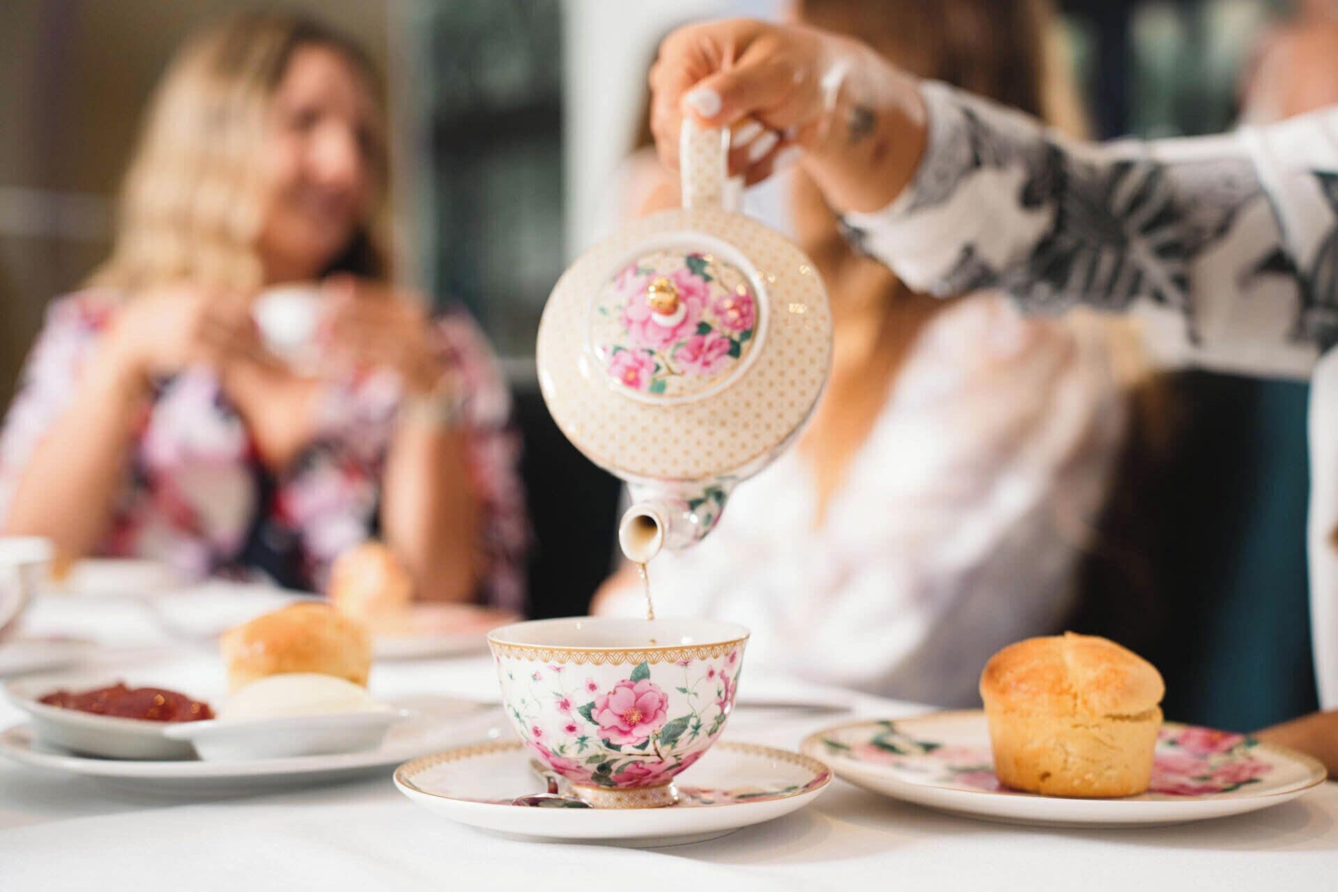 Alguém servindo chá numa xícara decorada com flores.