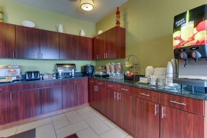 Cozinha com armários de madeira, máquina de café, dispensador de suco de frutas e diversos eletrodomésticos.