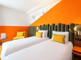Quarto de hotel com duas camas, uma mesa pequena e uma cadeira.