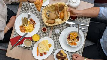 Uma mesa de café da manhã com pratos de comida, um bule e uma cesta de pão.