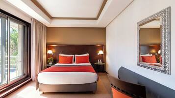Quarto de hotel com uma cama grande, duas mesas de cabeceira com luminárias, um espelho amplo e vista para palmeiras pela janela.