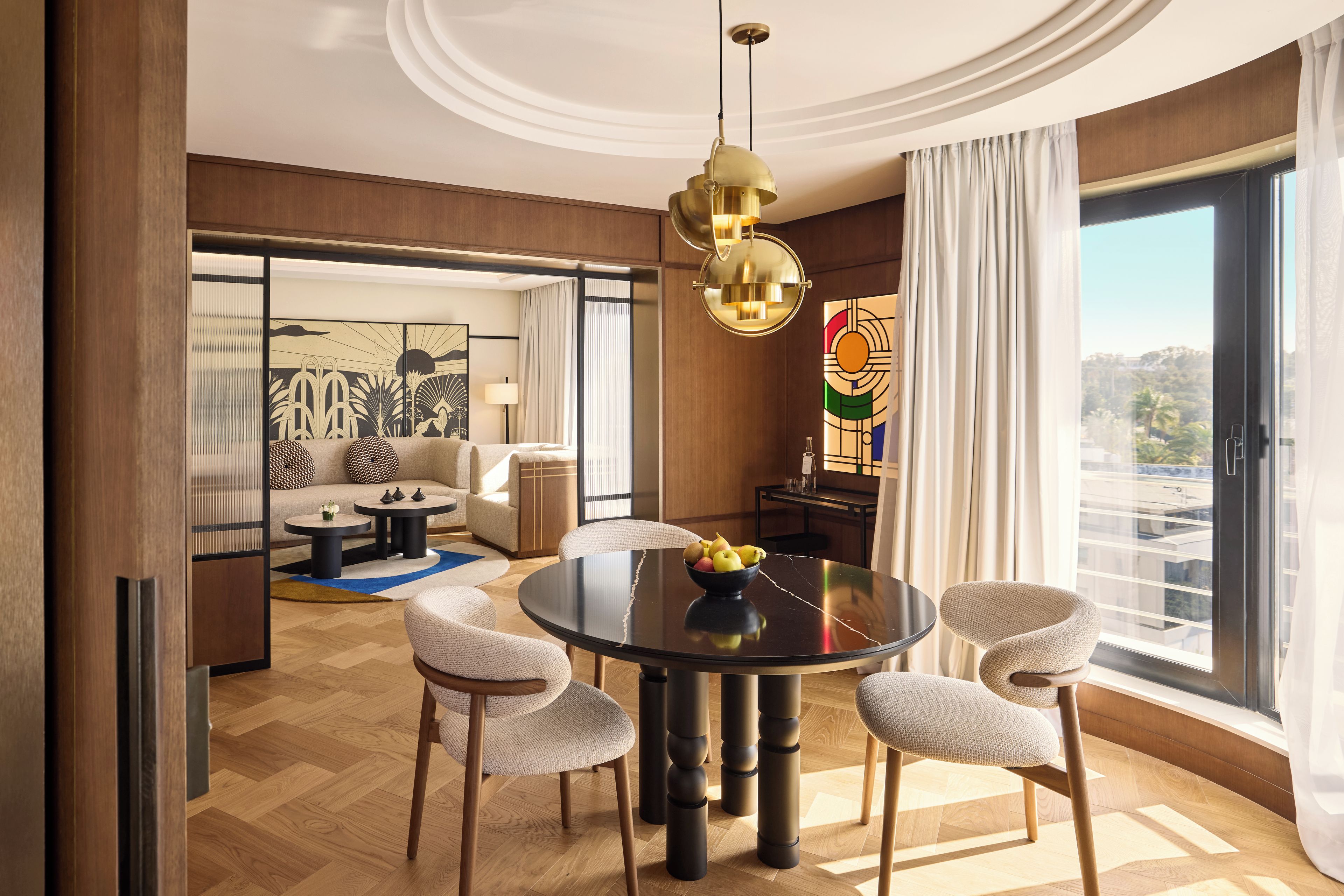 Uma sala de estar moderna com uma mesa de jantar redonda, duas cadeiras, um sofá e uma janela grande com cortinas.
