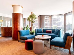 Uma área de estar moderna com um sofá azul, uma mesa de centro redonda e um banquinho vermelho.