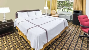 Quarto de hotel com uma cama grande, uma mesa, uma cadeira, uma janela com cortinas e um aquecedor.