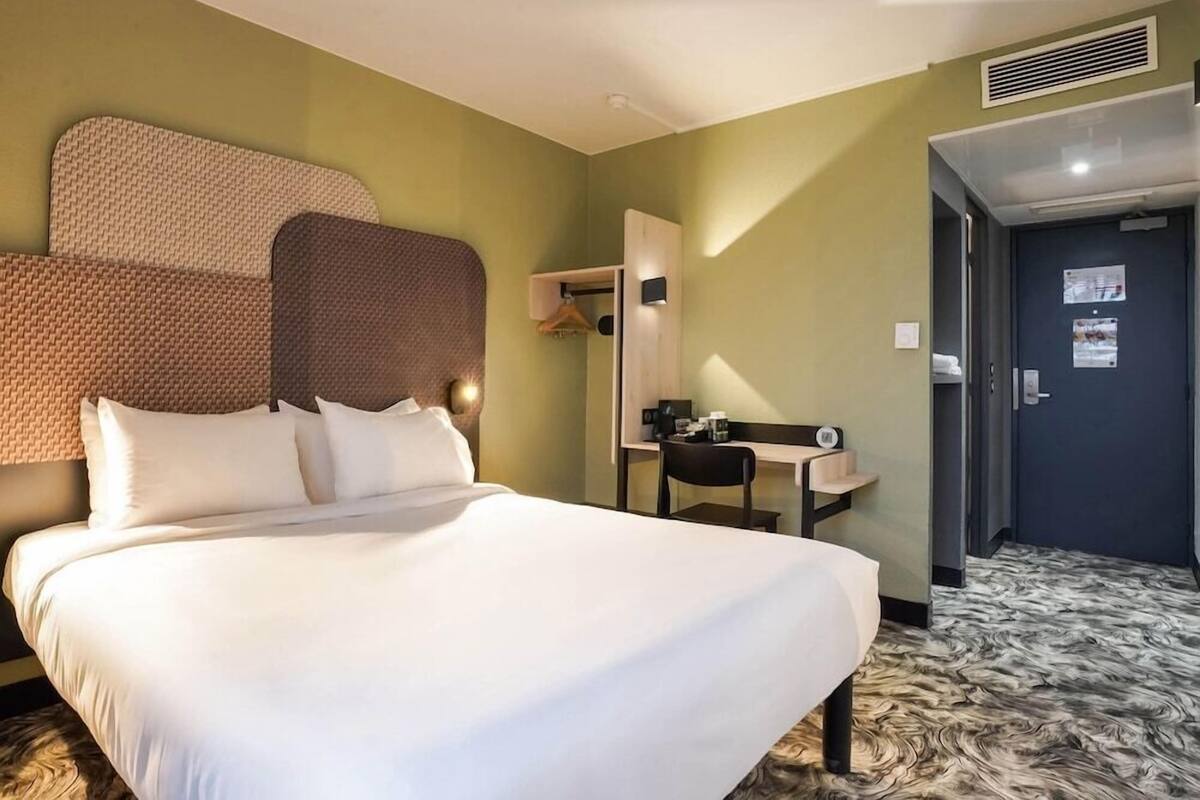 Quarto de hotel com uma cama grande, uma escrivaninha, um guarda-roupa e uma porta.