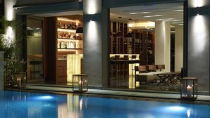 Uma área de piscina interior moderna, com bar e espaço para sentar, com estrutura de vidro e iluminação ambiente.