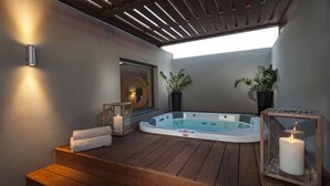 Uma área de spa com hidromassagem, degraus de madeira, velas e plantas em vasos.