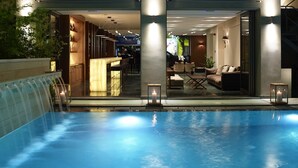 Uma área de piscina com bar e espaço para sentar, cercada por colunas e iluminação moderna.