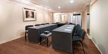 Uma sala de conferências com uma mesa comprida, cadeiras e um quadro na parede.