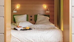 Cama com cabeceira de madeira, duas luminárias de cabeceira e uma bandeja com doces e uma xícara.