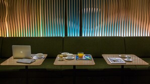 Uma área de refeições com um laptop, itens de café da manhã e uma revista sobre uma mesa.