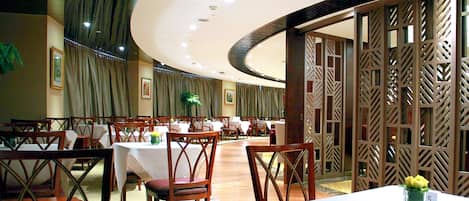 Um restaurante com mesas redondas, cadeiras de madeira e um painel decorativo.