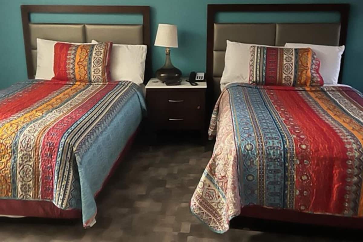 Duas camas com colchas estampadas, uma mesa de cabeceira com abajur e um telefone.