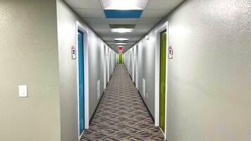 Corredor de hotel com piso coberto por carpete, portas em ambos os lados e uma câmera de segurança no teto.