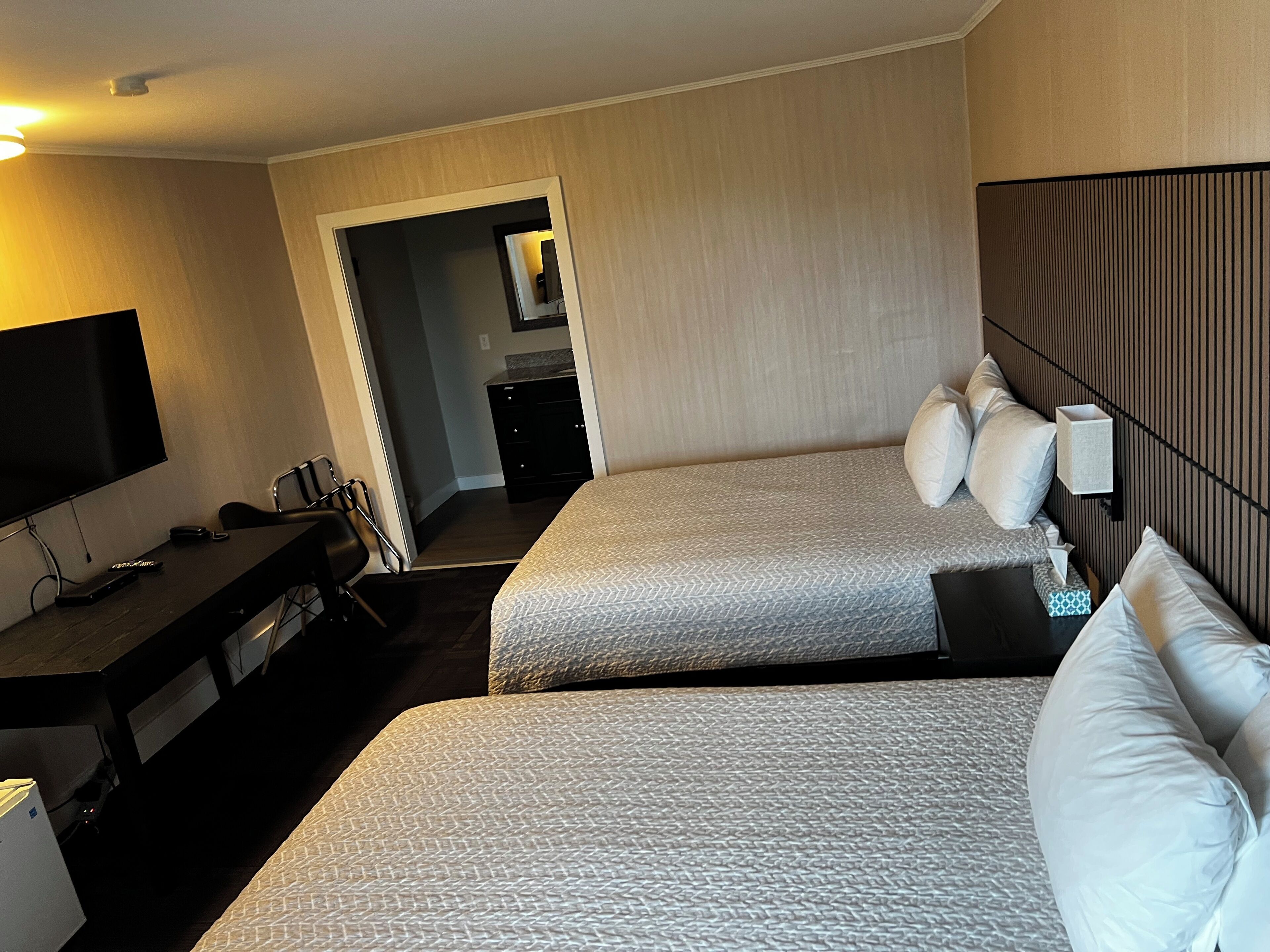 Quarto de hotel com duas camas, televisão, escrivaninha e espelho.
