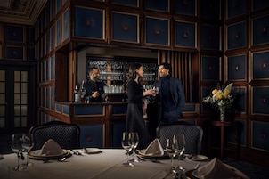 Uma área de bar com design em painéis de madeira escura, um balcão e um espaço com mesas preparadas para refeições.