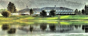 Um hotel grande, com vários andares, um telhado imponente e várias varandas, localizado à beira de um lago calmo com reflexos.