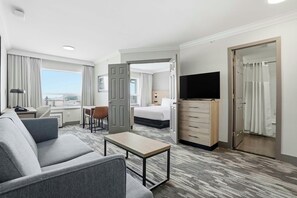 Quarto de hotel com sofá, uma mesa pequena, televisão, cama, escrivaninha e banheiro com cortina de chuveiro.
