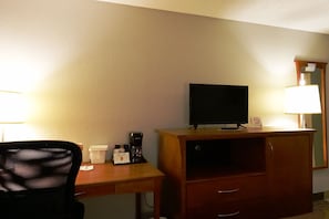 Quarto de hotel com uma escrivaninha de madeira, televisão, luminária e cafeteira.