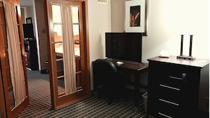 Quarto de hotel com escrivaninha, cadeira, cômoda, um quadro na parede e um tapete estampado.