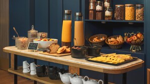 Um buffet de café da manhã com diversas opções de alimentos, incluindo frutas, pães e bebidas.