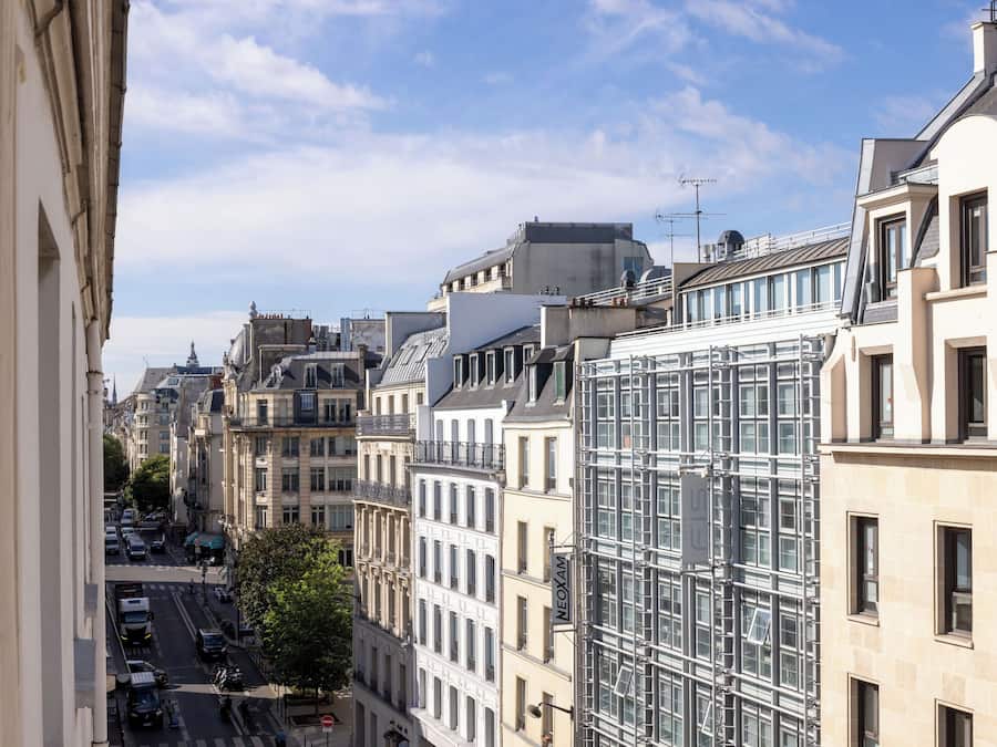 Rua urbana com edifícios históricos, uma estrutura moderna de vidro e céu claro.