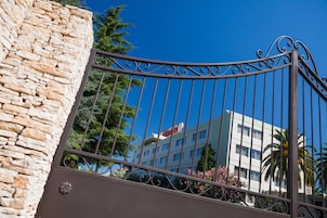 Um portão de metal com uma parede de pedra, um edifício com uma placa e árvores ao fundo.