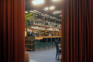 Uma área de bar com prateleiras cheias de garrafas e copos, um balcão com uma máquina de café e várias cadeiras.