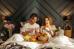 Um casal na cama com itens de café da manhã, uma câmera e um vaso de flores.