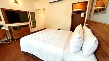 Quarto de hotel com cama, escrivaninha, cadeira, televisão e guarda-roupa.