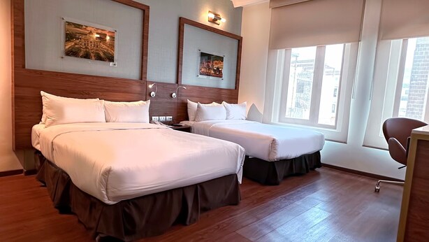 Quarto de hotel com duas camas, cabeceiras de madeira e janelas amplas.