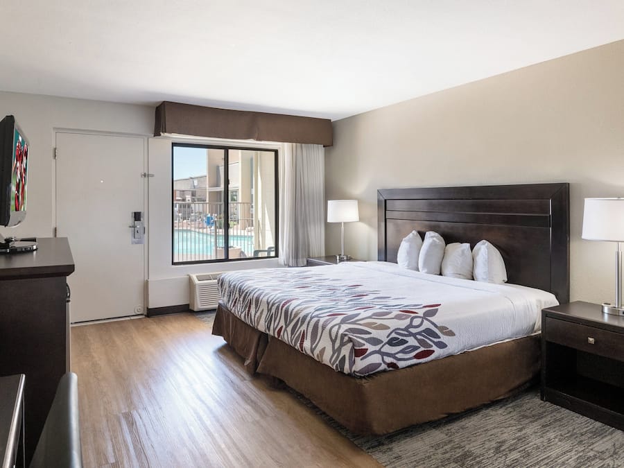 Quarto de hotel com uma cama grande, uma escrivaninha, televisão e janela com vista para edifícios.